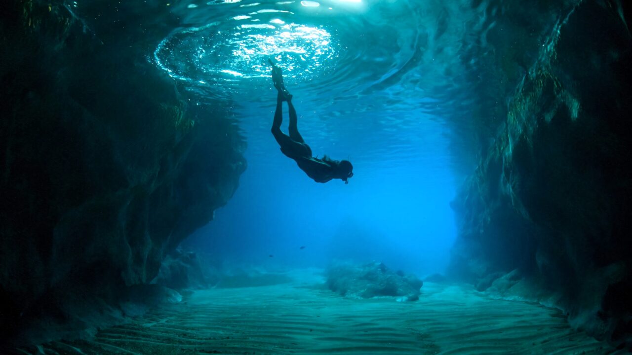 Graceful Woman Diving Amid Ocean Rocks in Crystal Blue Wallpaper ...