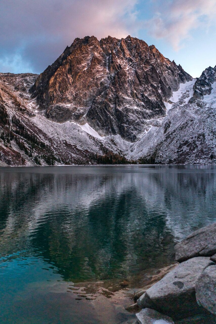 Snow-Capped Rocky Peak Reflected on Lake Shore Wallpaper | Background ...